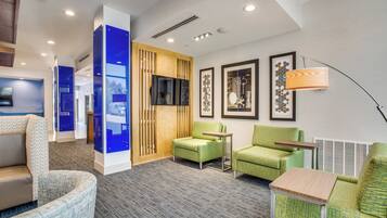 Um hall de hotel com áreas de estar, uma televisão de tela plana, obras de arte emolduradas e design moderno.