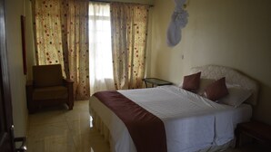 Quarto com cama, cadeira, mesa de cabeceira, cortinas e luminária pendente.