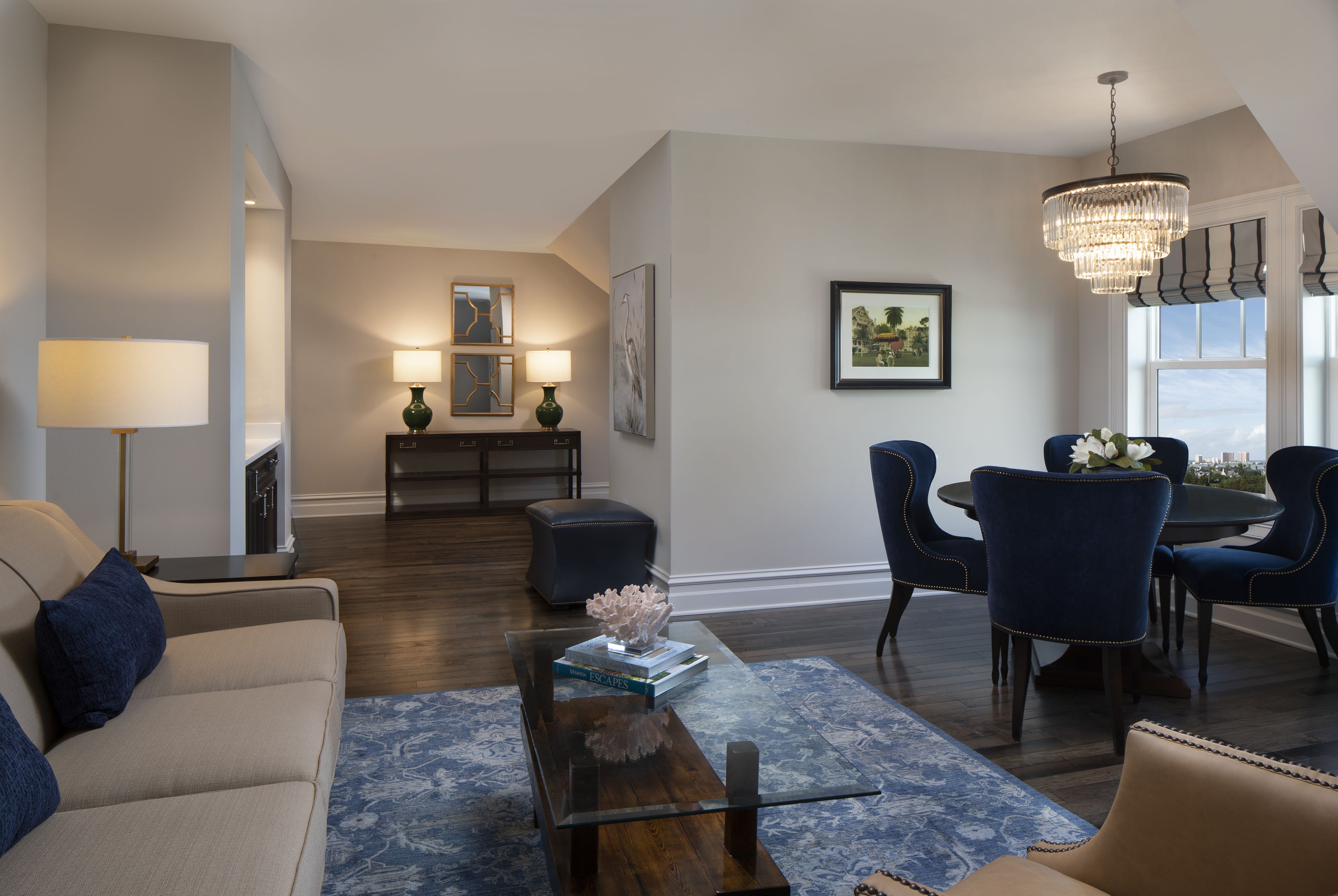 Uma sala de estar moderna com uma mesa de centro de vidro, cadeiras azuis e um lustre.