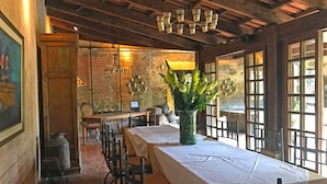 Uma sala de jantar com uma mesa comprida, cadeiras, um vaso com flores e uma parede de tijolos com lareira.