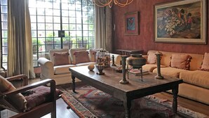 Uma sala de estar aconchegante com sofá, cadeiras, uma mesa de centro e uma janela grande com cortinas.