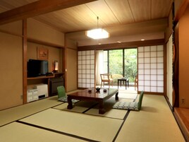 Um quarto japonês tradicional com tatames, uma mesa de madeira baixa, uma televisão e portas deslizantes que dão para uma varanda.