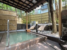 Uma área de águas termais com piscina azulejada, cercas de bambu e cadeiras de descanso.