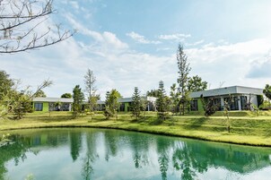 Uma área externa tranquila com um lago, edifícios verdes e árvores.