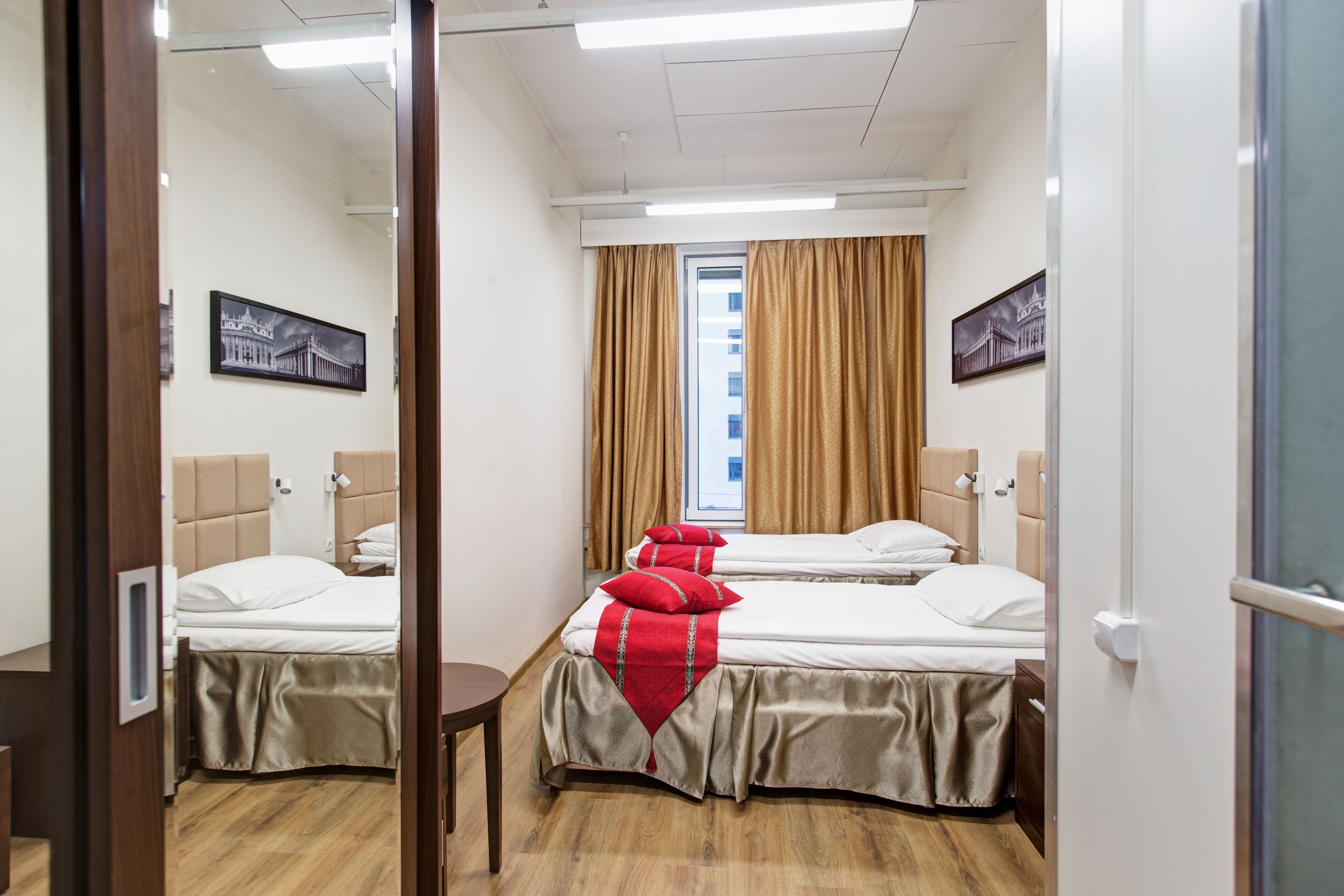 Quarto de hotel com duas camas, uma janela com cortinas e quadros nas paredes.