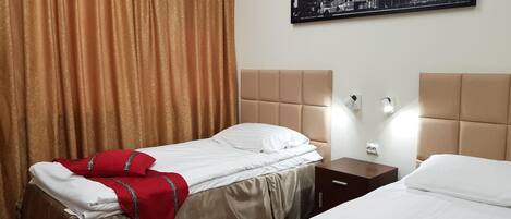 Quarto de hotel com duas camas, vista para a cidade, cortina e mesa de cabeceira com abajur.