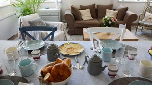 Uma área de refeições com uma mesa posta para o café da manhã, incluindo croissants, uma pilha de panquecas e diversas xícaras e canecas.