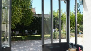 Uma estufa com vista para um jardim, uma mesa com uma vela e uma cadeira.