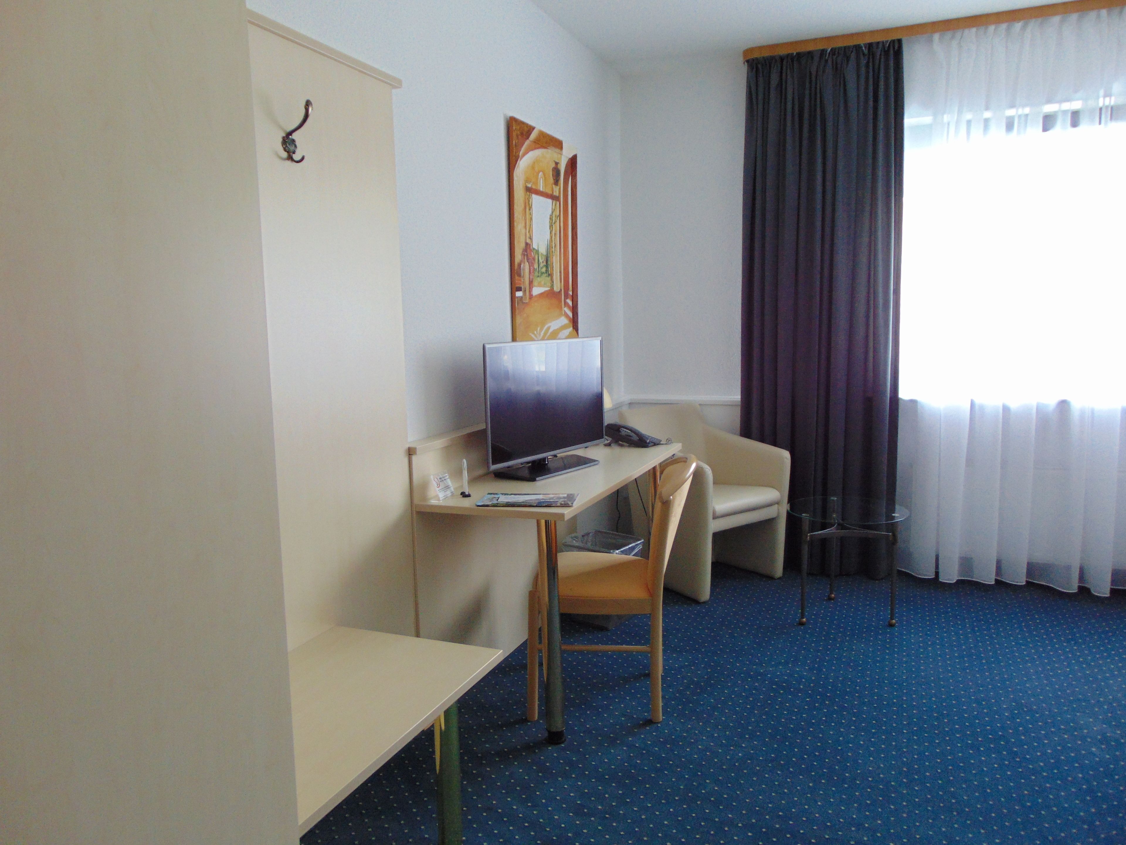 Quarto de hotel com escrivaninha, cadeira e televisão.