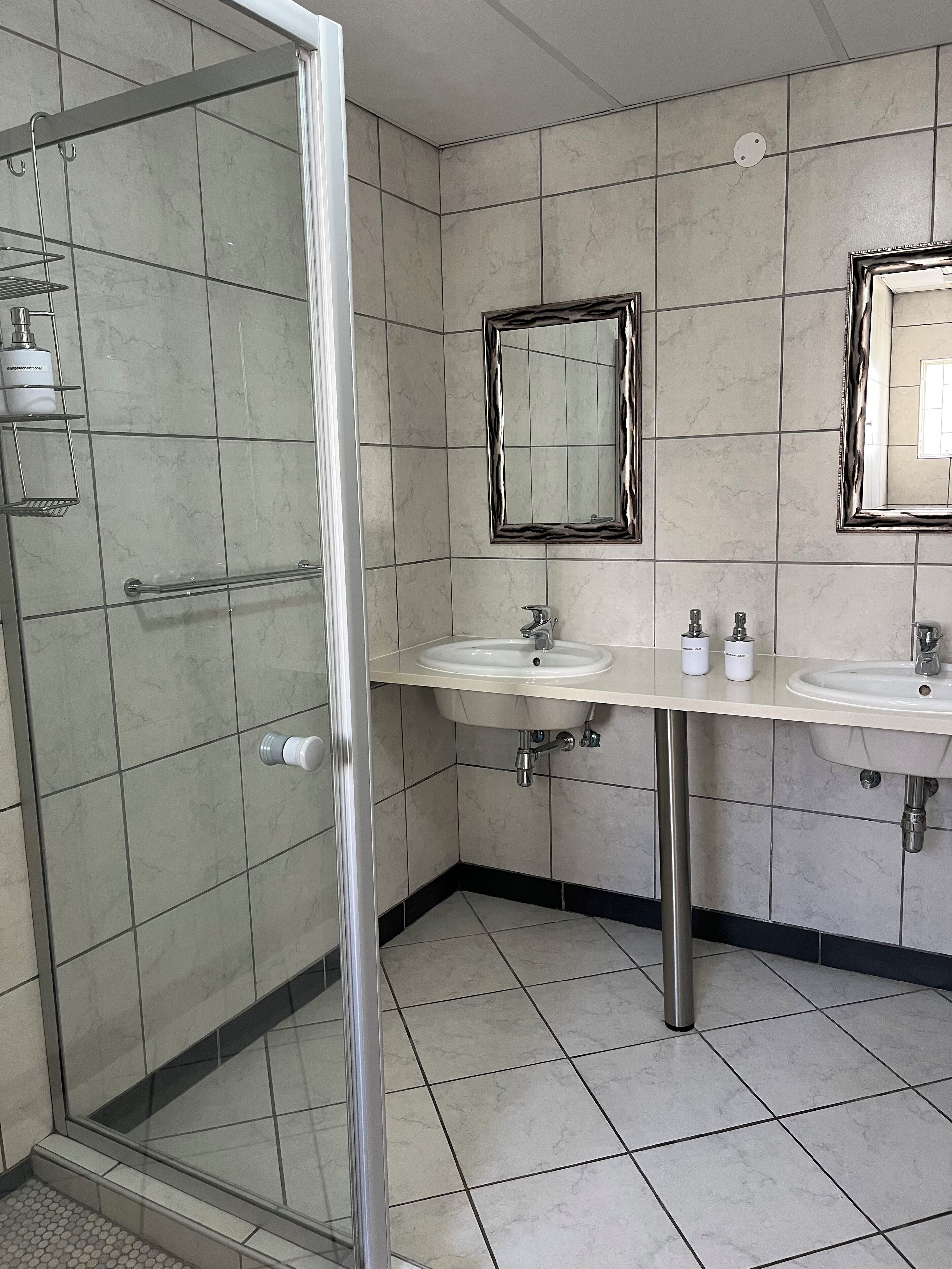 Um banheiro moderno com box de vidro, duas pias e dois espelhos.