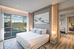 Quarto de hotel moderno com uma cama grande, um quadro sobre a cabeceira, vista para uma piscina e área de banheiro separada.