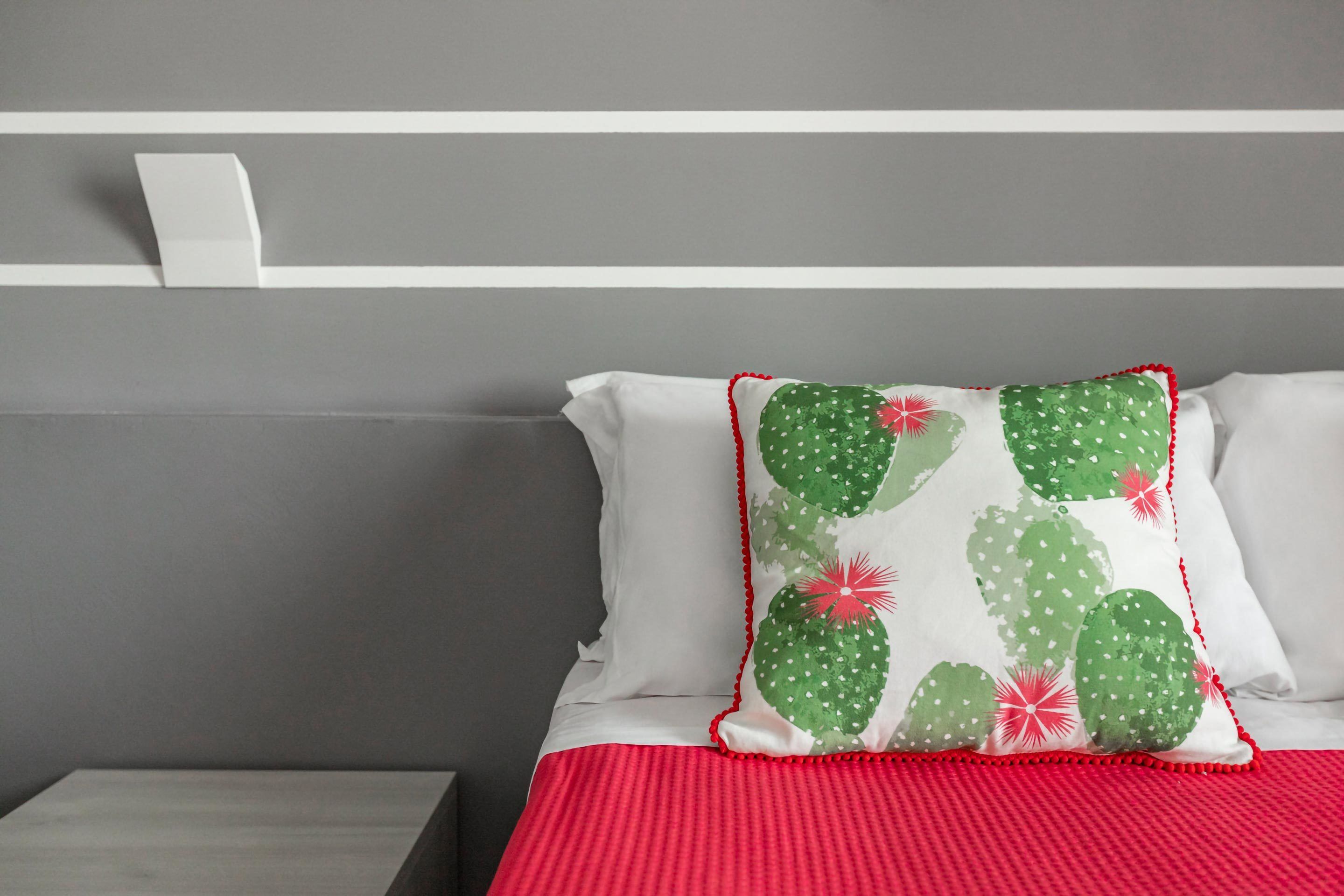 Uma cama com um cobertor vermelho e um travesseiro com padrão de cactos.