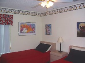 Quarto com duas camas, ventilador de teto e quadros nas paredes.