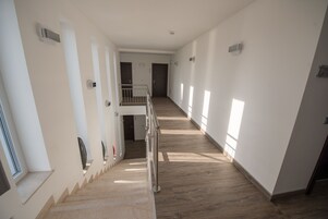 Um corredor amplo e bem iluminado, com piso de madeira, corrimão de metal e escada que leva a um segundo andar.