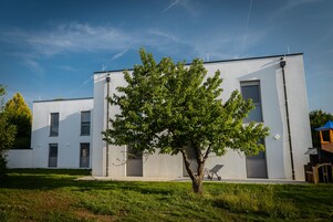 Um edifício moderno com telhado plano, janelas grandes e uma árvore em primeiro plano.