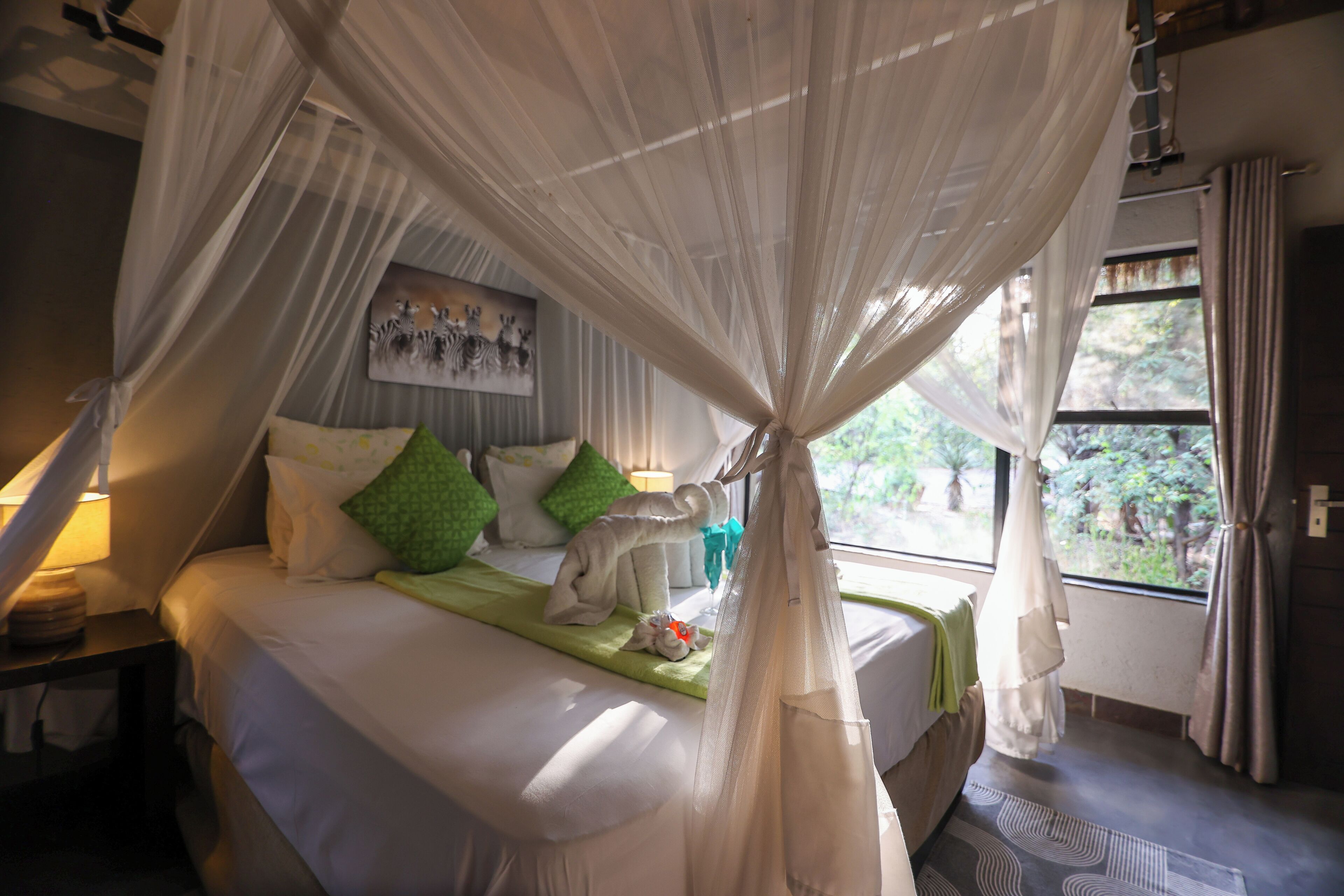 Quarto com cama de dossel, travesseiros verdes, mesa de cabeceira e janela com cortinas.