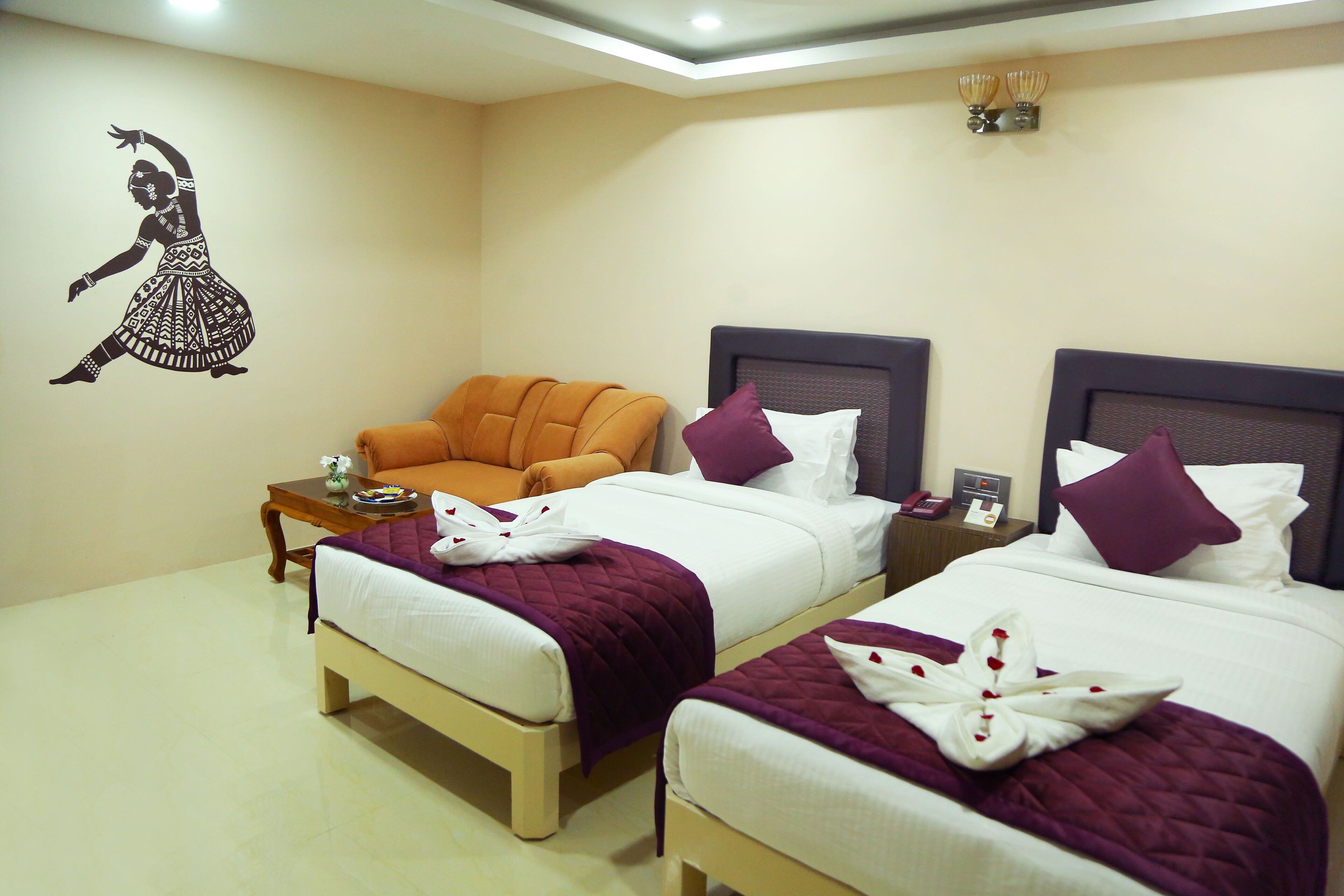 Quarto de hotel com duas camas, uma mesinha de cabeceira, uma cadeira e um objeto decorativo na parede.