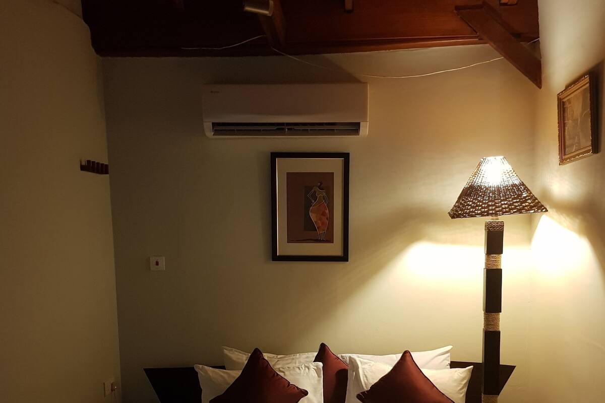 Um quarto com uma cama, almofadas, uma moldura na parede e um abajur.