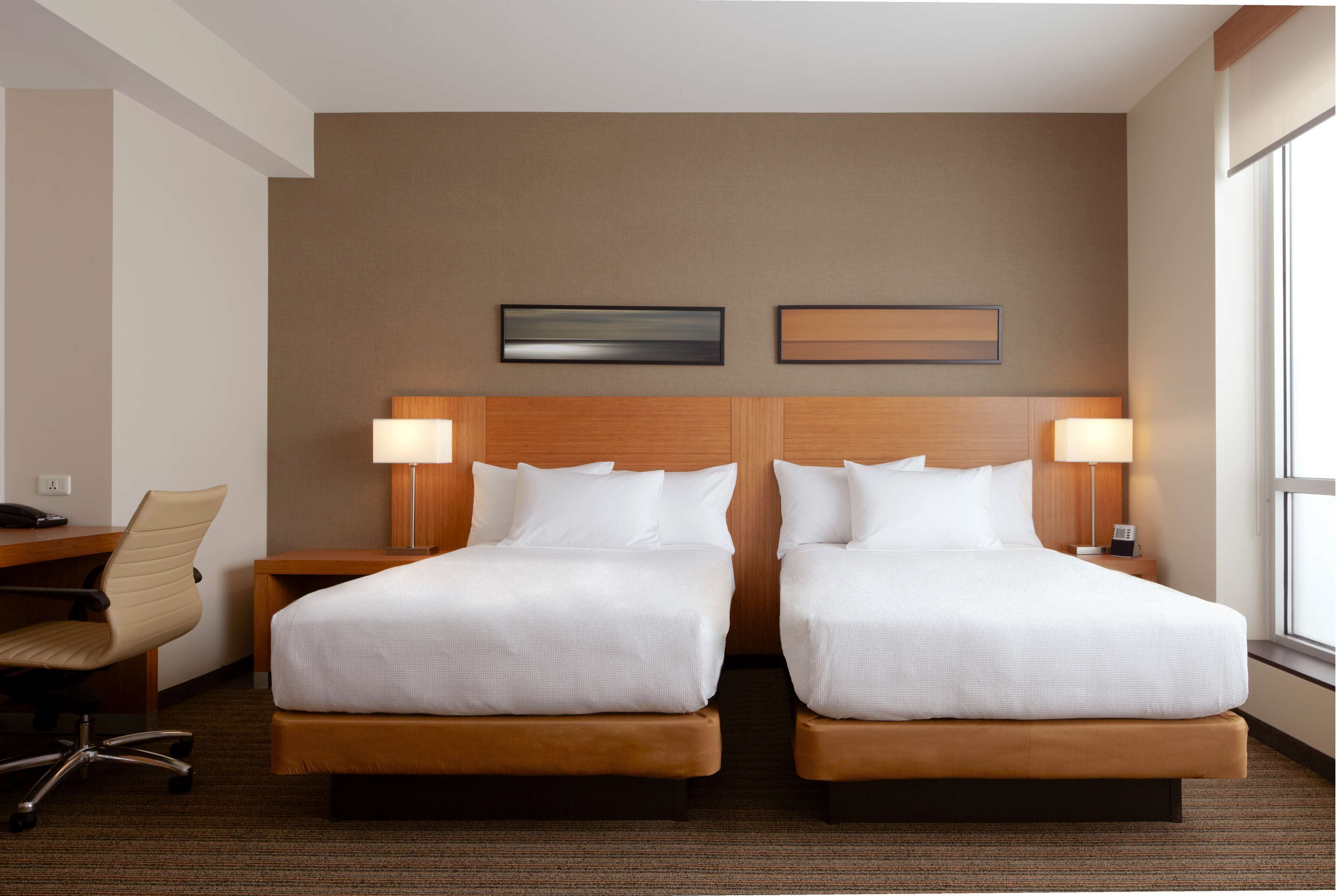 Quarto de hotel com duas camas, uma escrivaninha e uma cadeira.
