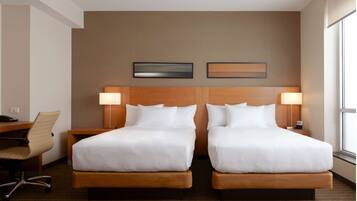 Quarto de hotel com duas camas, uma escrivaninha e uma cadeira.