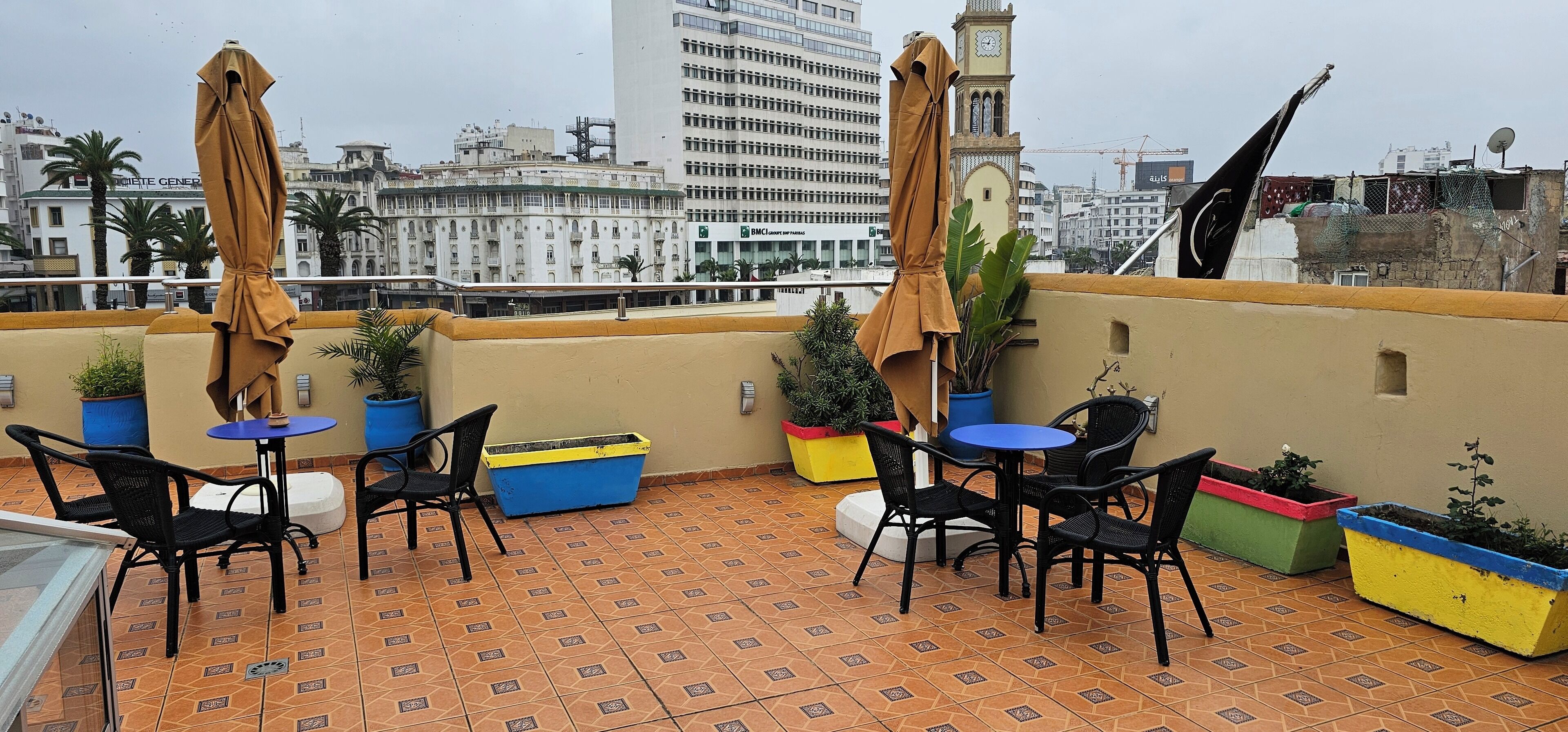Terraço no telhado com área de estar externa, plantas em vasos e vista para prédios da cidade.