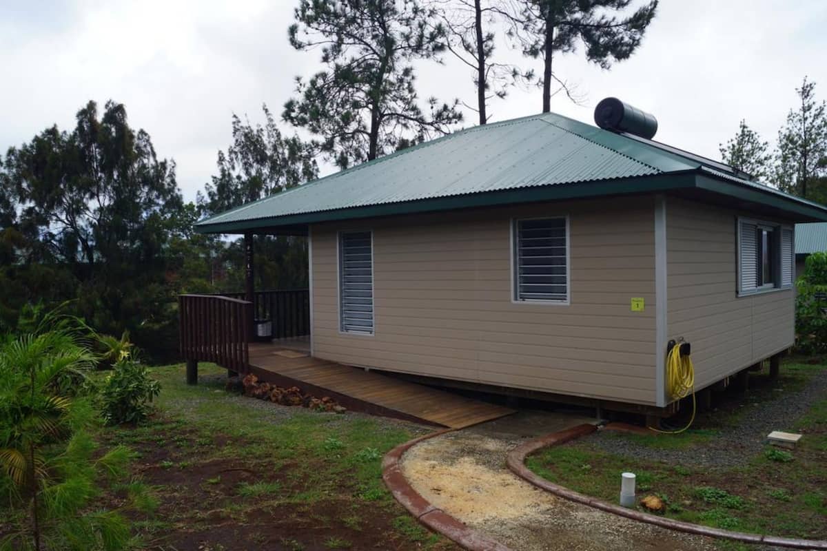 Uma casa térrea com telhado verde, um pequeno alpendre e uma mangueira visível.