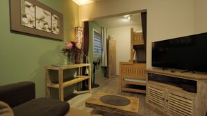 Uma sala de estar com televisão, móveis de madeira, uma mesa pequena e um vaso decorativo.