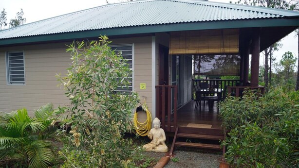 Uma casa com varanda coberta, uma pequena estátua e um jardim com diversas plantas.