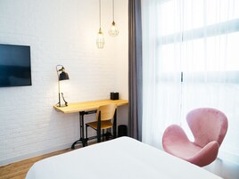 Quarto moderno com escrivaninha de madeira, uma cadeira, uma cama e uma poltrona rosa.