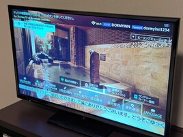 Um ecrã de televisão mostra um quarto de hotel com uma parede de tijolos, um pilar de pedra e um chão em mosaico.