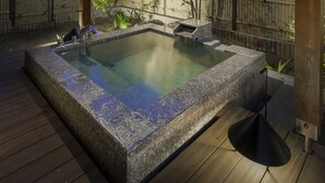 Uma banheira de hidromassagem numa área de deck de madeira, com um cercado de bambu ao fundo.