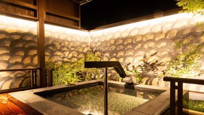 Piscina ao ar livre aquecida com um muro de pedra ao fundo, um deck de madeira e um guarda-corpo de metal.