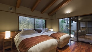 Quarto com cama grande, vigas de madeira, porta de correr de vidro e mesa de cabeceira com abajur.