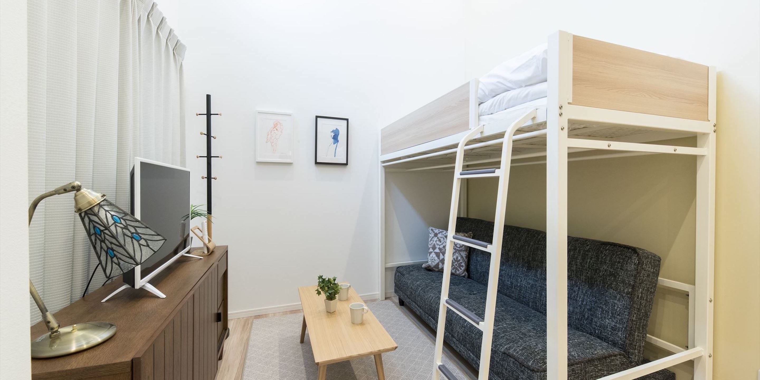 Quarto com beliche, escrivaninha, computador e pequena mesa com uma planta.