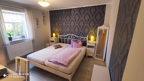 Quarto bem arrumado com cama, mesas de cabeceira, espelho e janela com cortinas.
