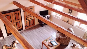 Uma sala de estar ampla com vigas de madeira, uma televisão, um sofá e um balanço de cavalo.