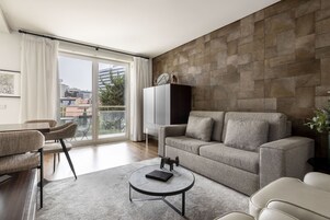 Uma sala de estar moderna com um sofá cinzento, uma mesa de centro redonda e um espaço de refeições com um banco e cadeiras.