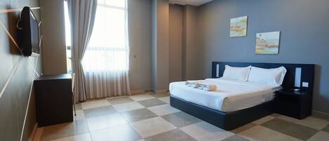 Quarto de hotel com cama, televisão, escrivaninha e janela com cortinas.