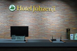 Bancada de recepção no Hotel Johzenji, com parede de tijolos ao fundo, um logotipo e algumas placas informativas.