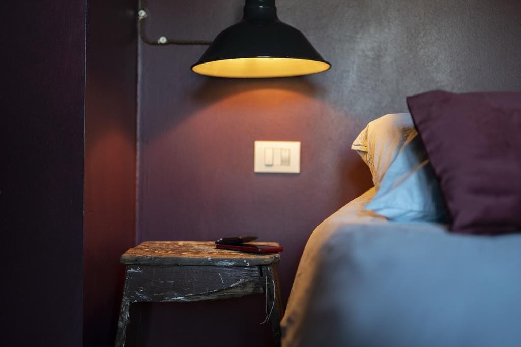 Quarto com cama, mesa de cabeceira, abajur e tomada.