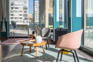 Uma sala de estar moderna com uma janela grande, uma mesa de madeira redonda e um espaço de estar aconchegante.