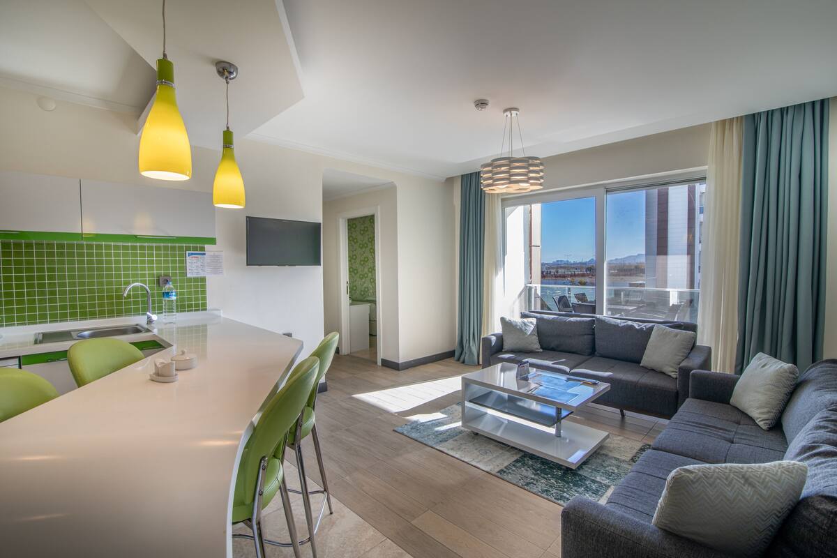 Uma sala de estar moderna com uma janela grande, um sofá, uma mesa de centro e uma área de cozinha com balcão.