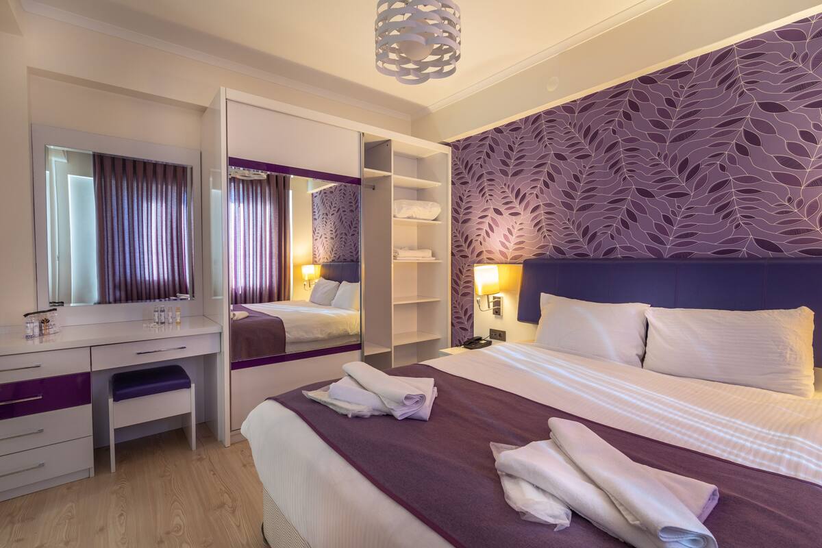 Quarto de hotel com cama, escrivaninha, espelho e guarda-roupa.
