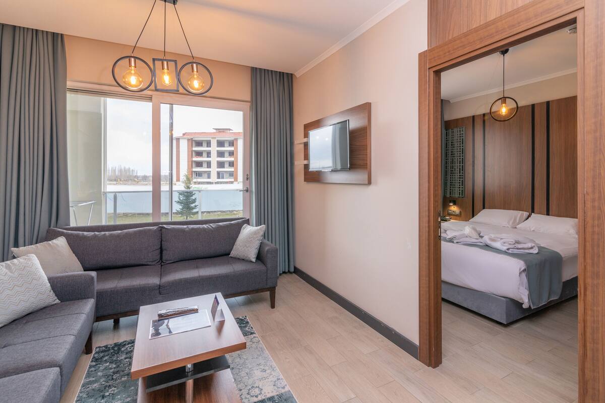 Quarto de hotel moderno com sofá, cama, televisão na parede e vista para a paisagem urbana.
