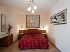 Quarto com cama de madeira, uma obra de arte floral acima da cama, um quadro na parede e um vaso com flores em uma mesa de cabeceira.