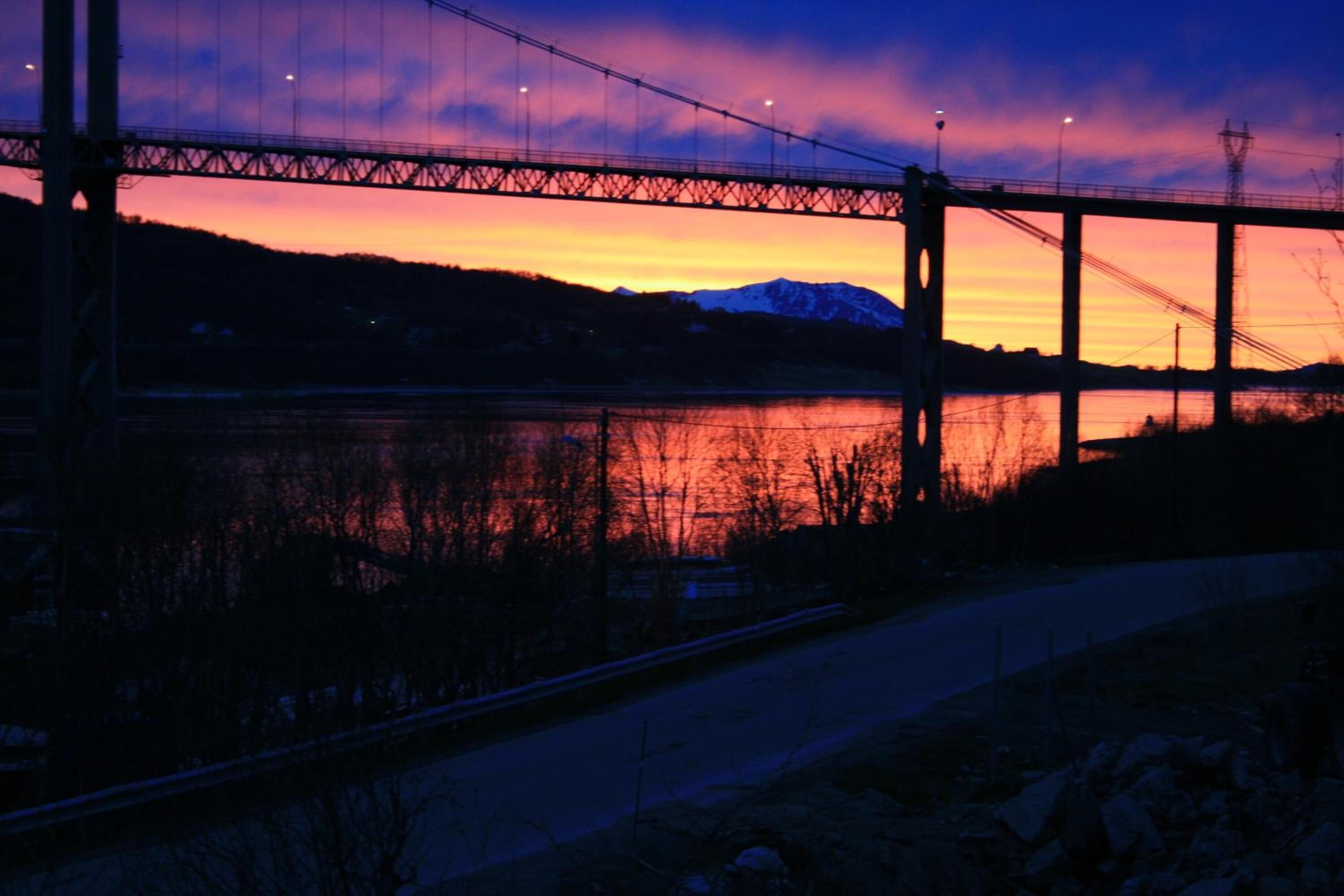 Uma ponte suspensa ao pôr do sol, com uma montanha ao fundo.