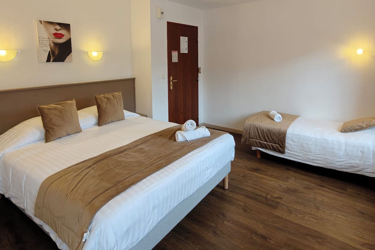 Quarto de hotel com uma cama grande, uma cama menor, piso de madeira e luminárias fixadas na parede.