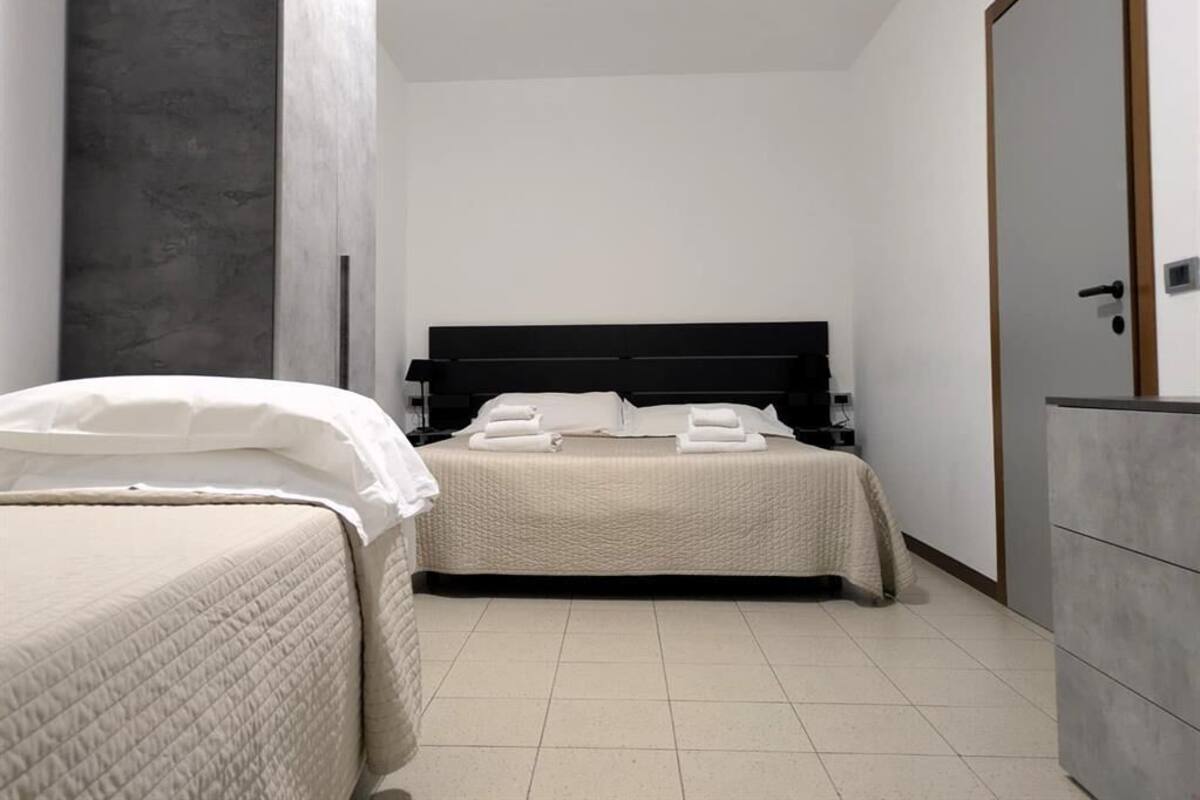 Quarto moderno com duas camas, um guarda-roupa e uma cabeceira escura.