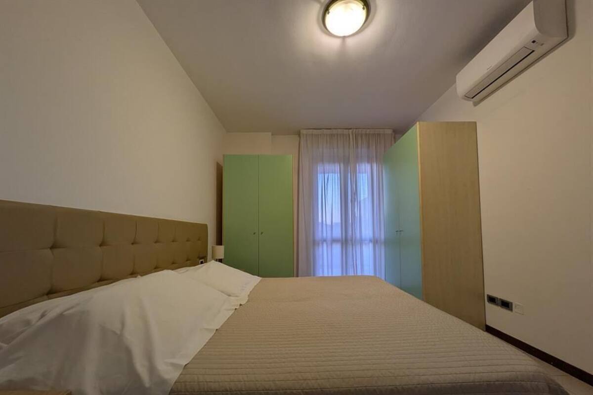 Quarto com cama, mesa de cabeceira, guarda-roupa e ar condicionado.