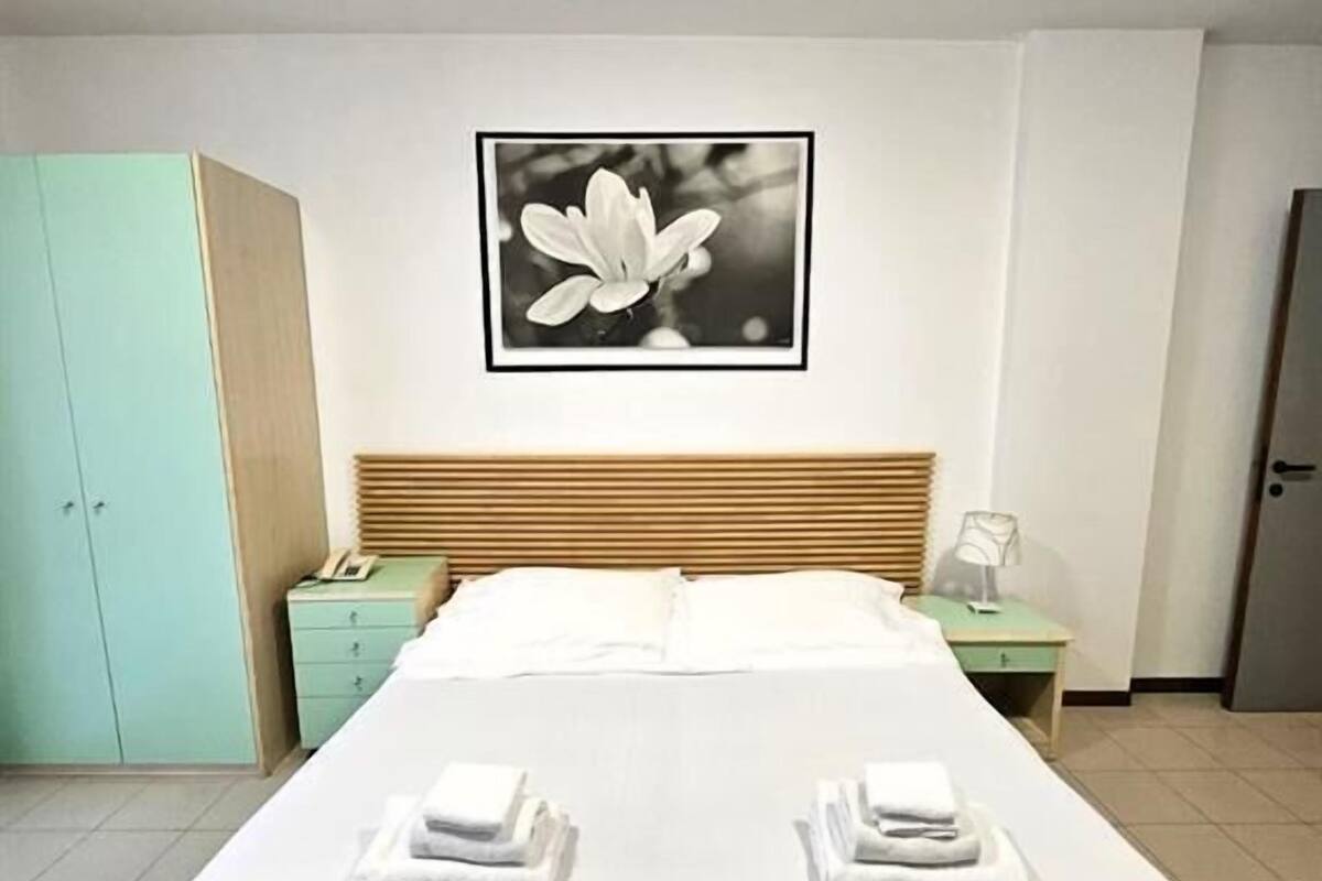 Quarto de hotel com uma cama, mesa de cabeceira, guarda-roupa e um quadro na parede.